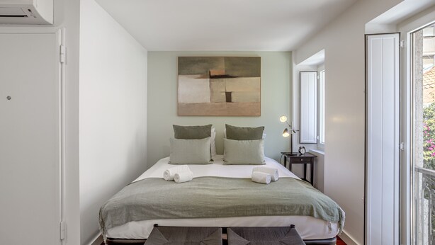 Quarto com cama, almofadas, mesa de cabeceira e uma janela.