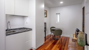 Uma cozinha compacta com fogão embutido, pia e armários brancos. Há um espaço de jantar com mesa e cadeiras, e uma pequena janela que traz luz natural.