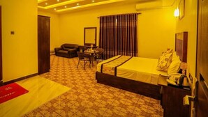 Quarto de hotel com cama, escrivaninha, cadeira e sofá.