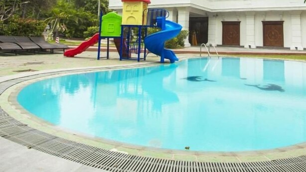 Piscina com área de recreação, edifício de vários andares com arquitetura clássica e céu limpo.