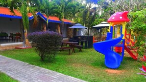 Área de recreação infantil com escorrega, mesas de piquenique e área de estar coberta.