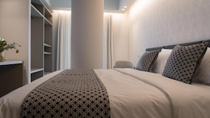 Quarto de hotel com cama, mesa de cabeceira, espelho, guarda-roupa e janela com cortinas.
