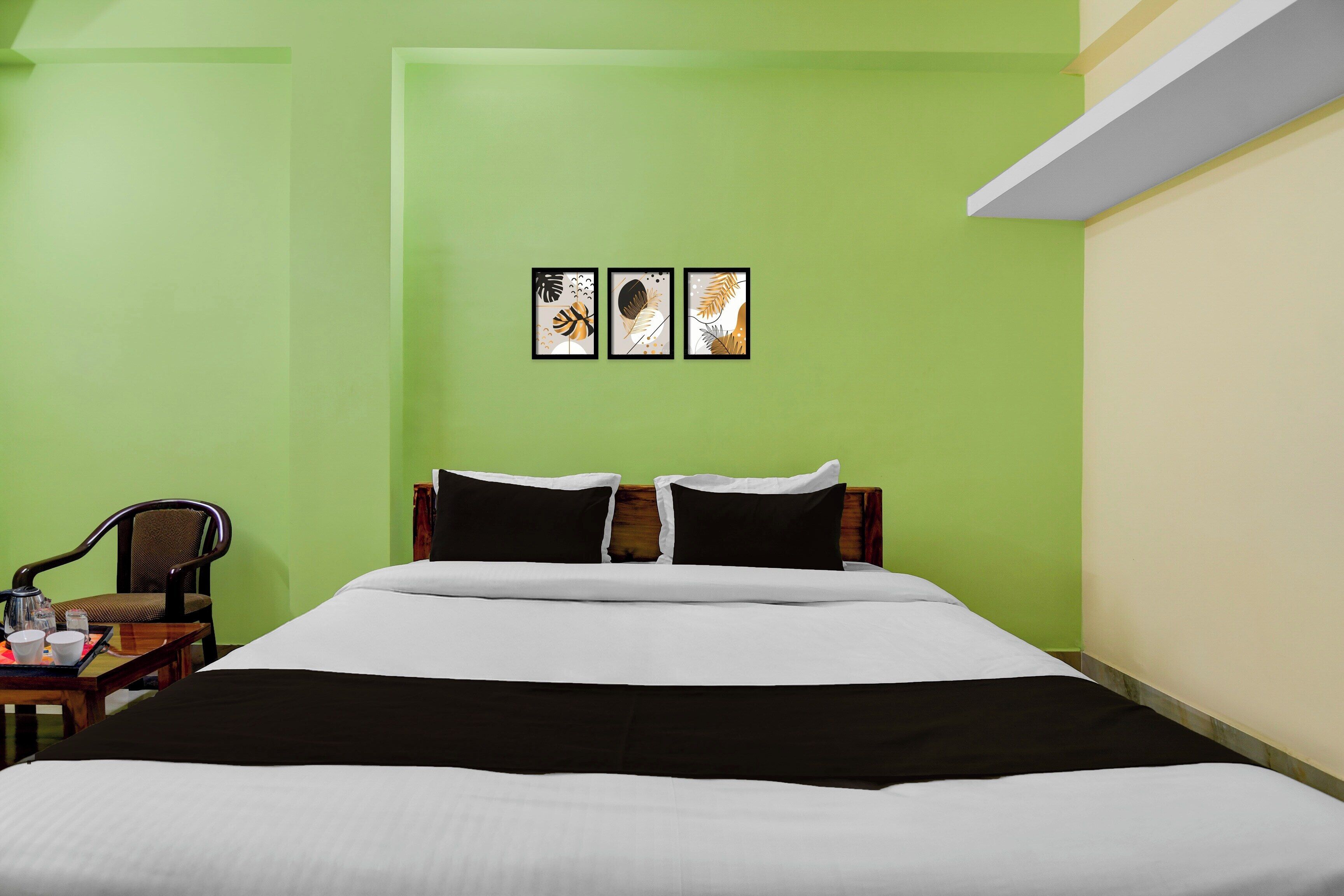 Quarto de hotel com uma cama, duas almofadas, uma cadeira, uma mesinha com bandeja e três quadros na parede.