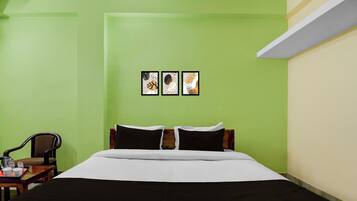 Quarto de hotel com uma cama, duas almofadas, uma cadeira, uma mesinha com bandeja e três quadros na parede.