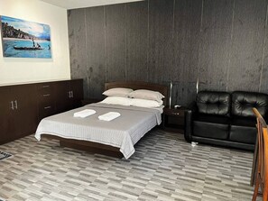 Um quarto com uma cama, uma poltrona de couro preto, um guarda-roupa de madeira e um quadro na parede.
