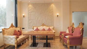 Um quarto luxuoso com piso de mármore, sofás ornamentados, uma mesa central e painéis decorativos nas paredes.