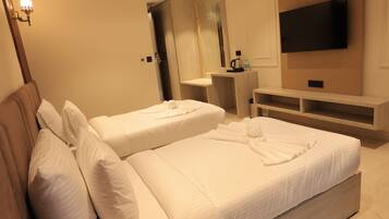 Quarto de hotel com duas camas, televisão, espelho e pequena escrivaninha com chaleira e garrafas.