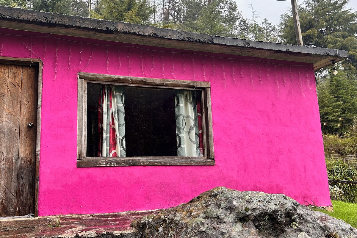 Um edifício rosa com porta de madeira e janela com cortinas.