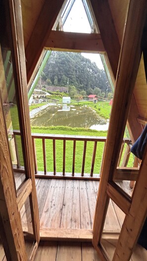 Um deck de madeira com guarda-corpo, vista para um lago e um morro arborizado ao fundo.