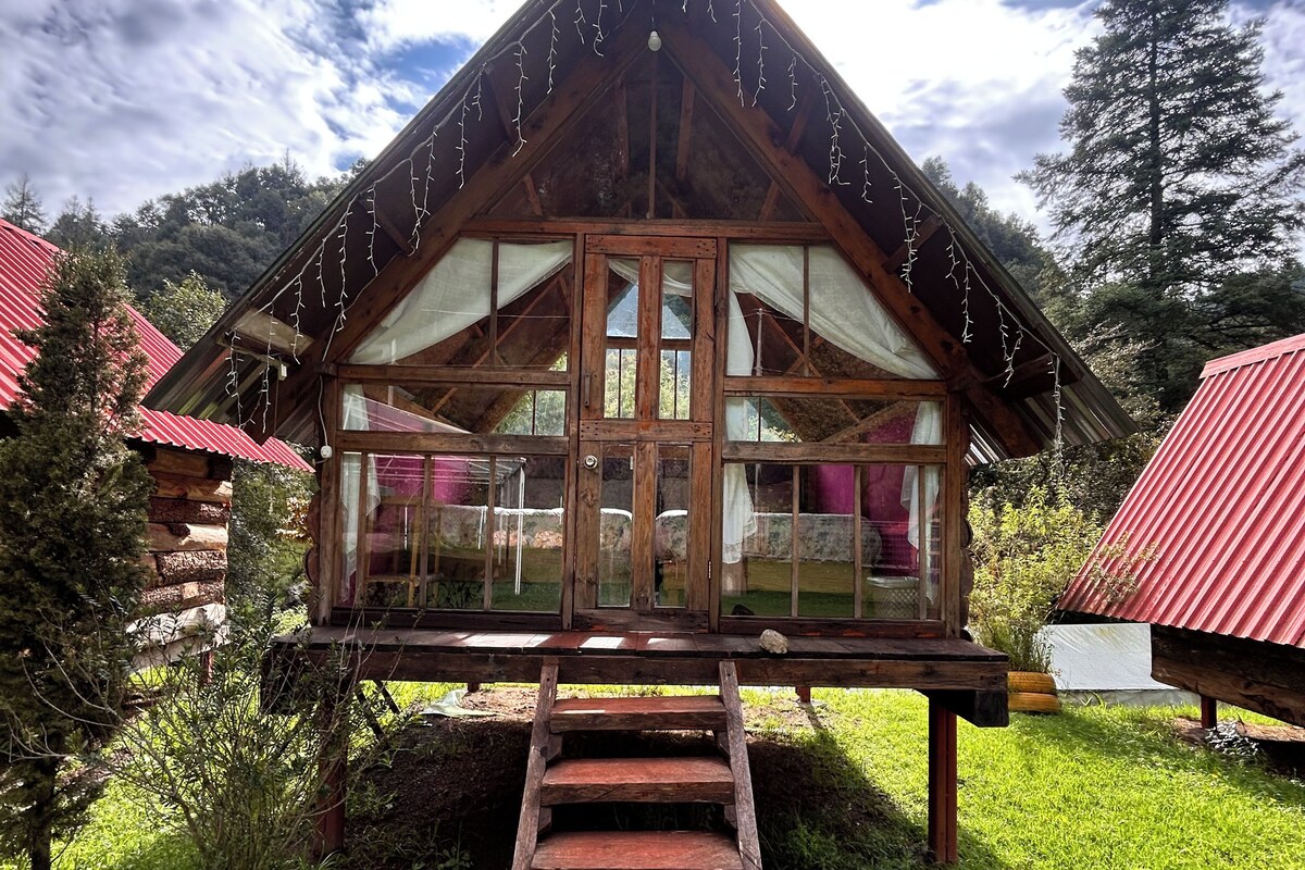 Uma cabana de madeira com varanda, escadas de madeira e telhado vermelho.
