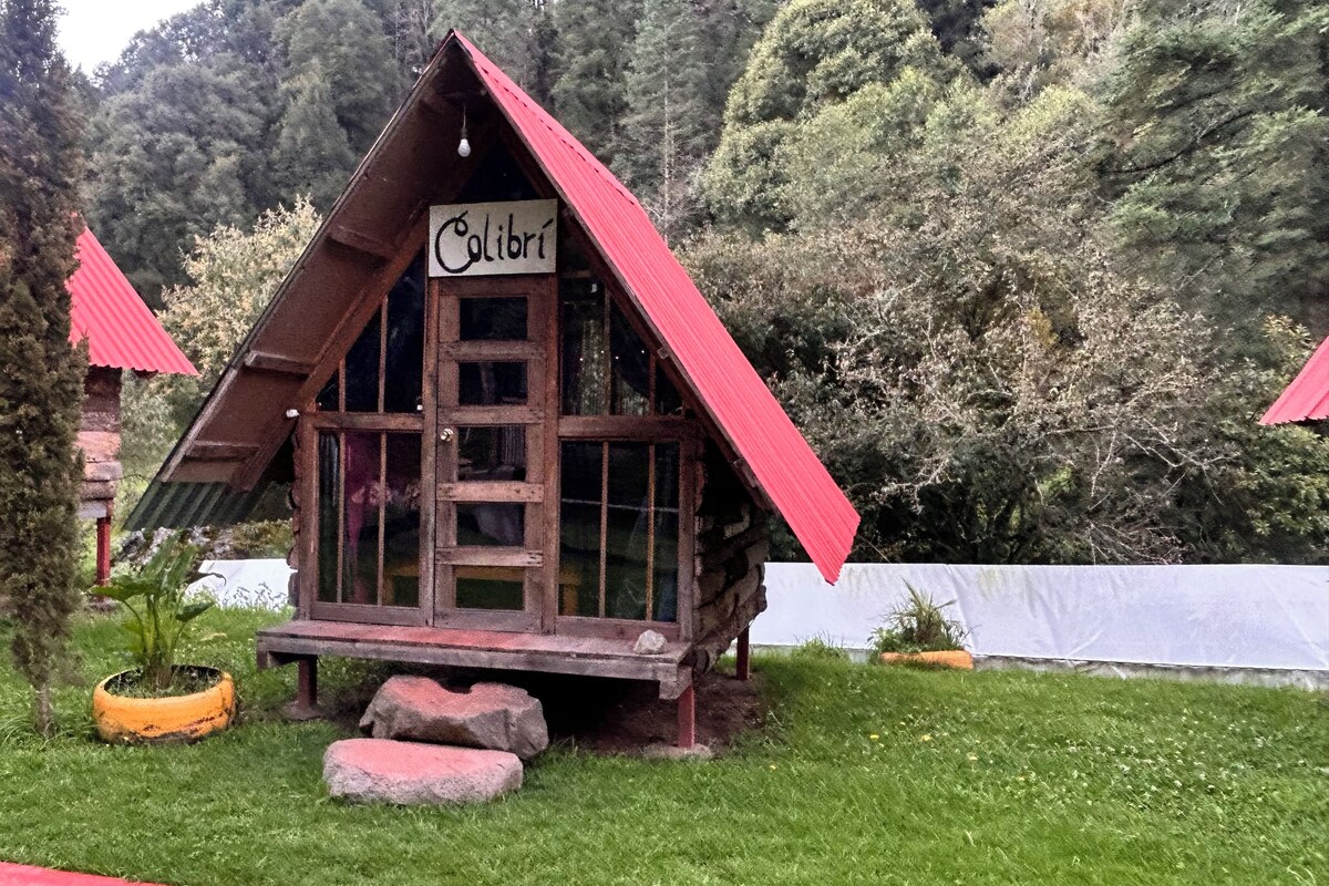 Uma cabana de madeira rústica com telhado vermelho e uma placa com a inscrição 'Calibrí'.