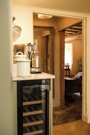 A kitchen area with a coffee machine, a refrigerator, and a wooden door leading to a dining area.