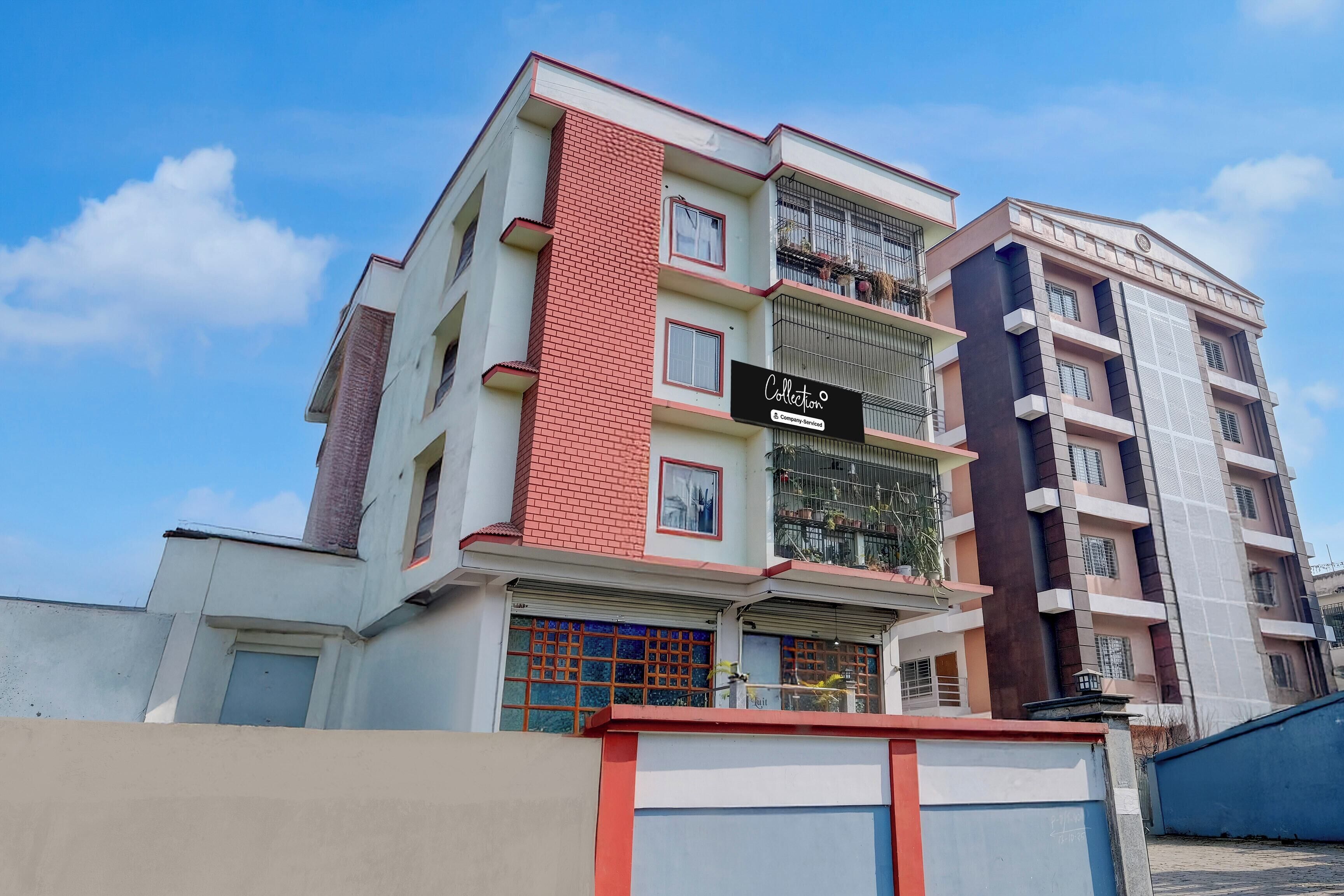 Um edifício residencial de vários andares com uma fachada de tijolos vermelhos marcante, varandas com guarda-corpos de metal e um letreiro indicando 'Collection' e 'Company-Serviced'.