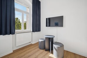 Quarto moderno com uma janela ampla, TV de tela plana na parede e dois pufes redondos.