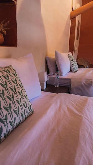 Quarto de hotel com duas camas, uma cabeceira de madeira e uma mesinha com uma garrafa.