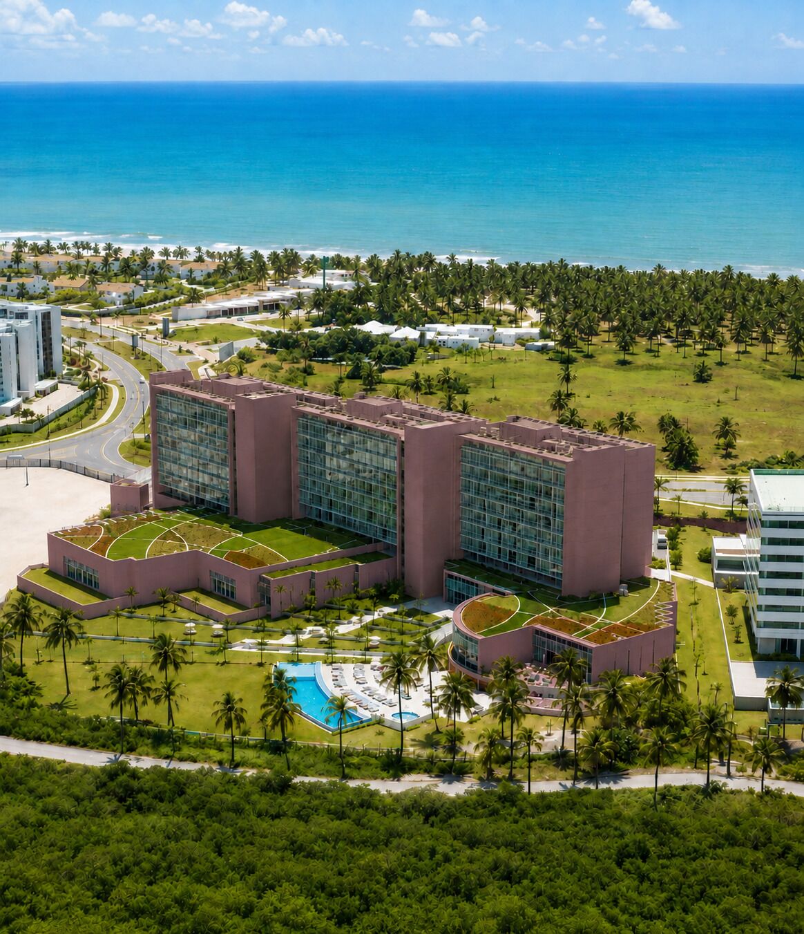 Um grande hotel com vários edifícios, piscina e vista para o oceano.