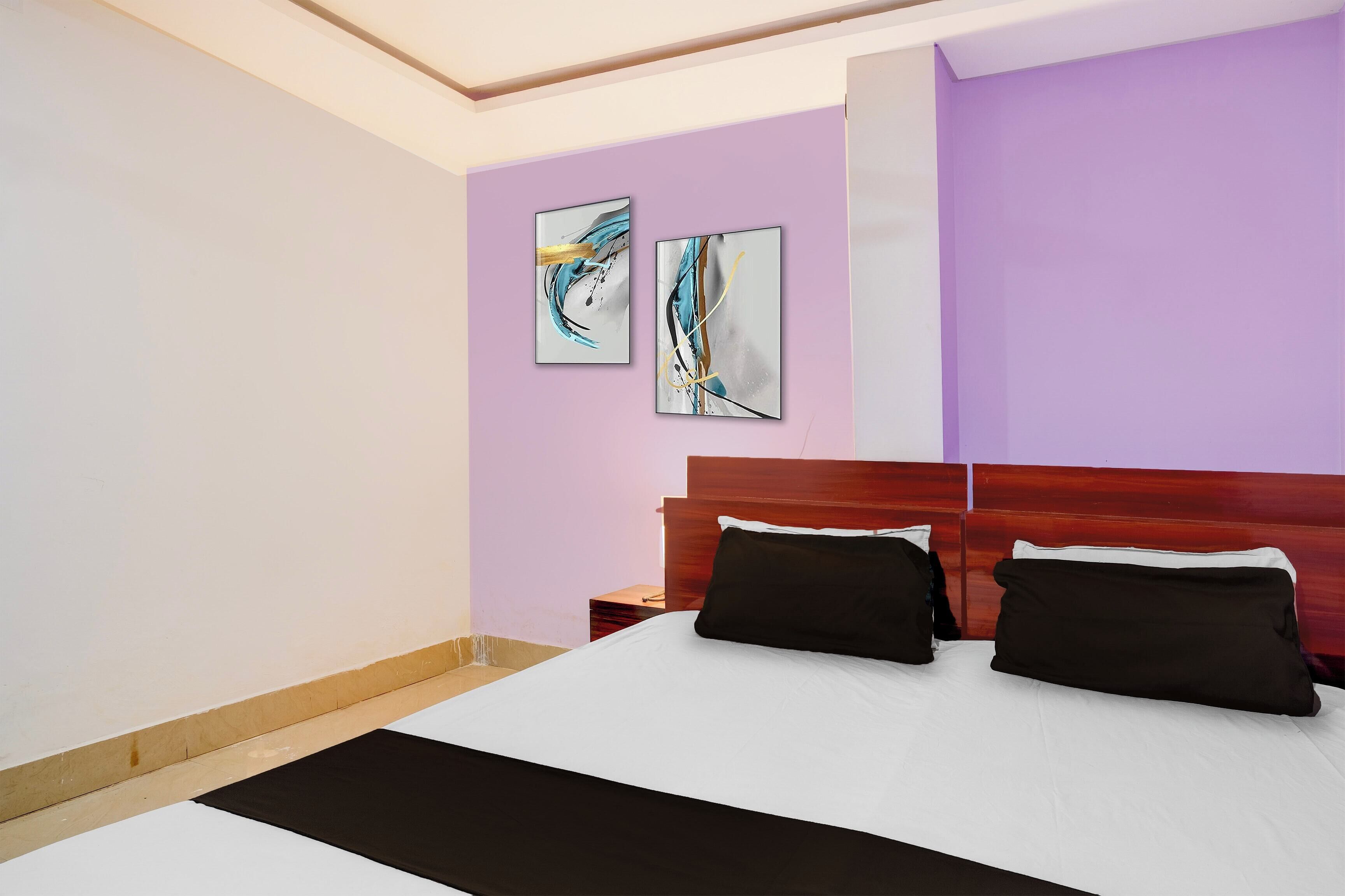 Quarto com uma cama, duas almofadas, uma mesa de cabeceira e duas pinturas abstratas na parede.
