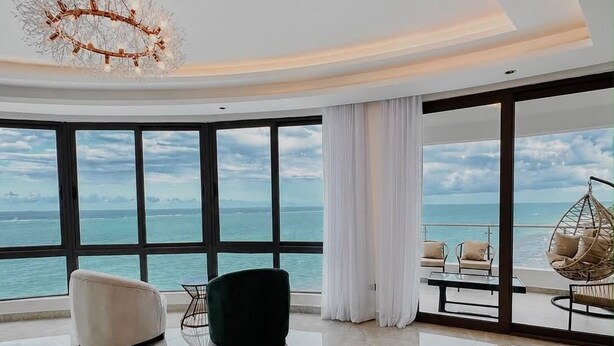 Um quarto espaçoso com uma ampla vista do oceano, um lustre e uma cadeira suspensa.