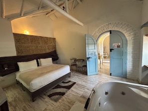 Quarto com cama grande, área de estar com mesa e cadeiras, e banheiro com banheira.