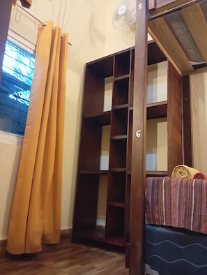 Quarto com estante de madeira, janela com cortinas e cama com manta listrada.