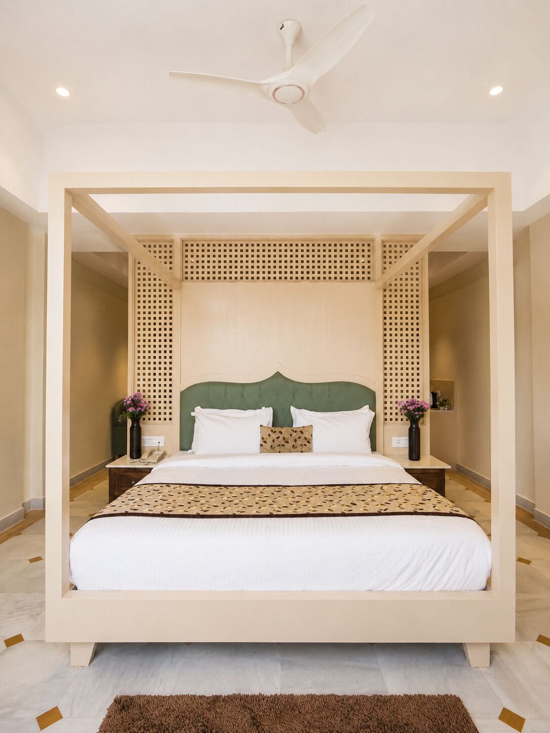 Uma cama de dossel com cabeceira estofada verde, roupa de cama branca e um corredor decorativo.