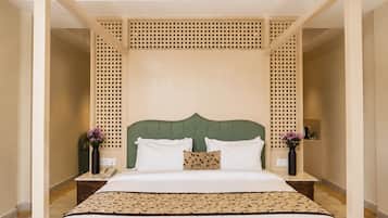 Uma cama de dossel com cabeceira estofada verde, roupa de cama branca e um corredor decorativo.