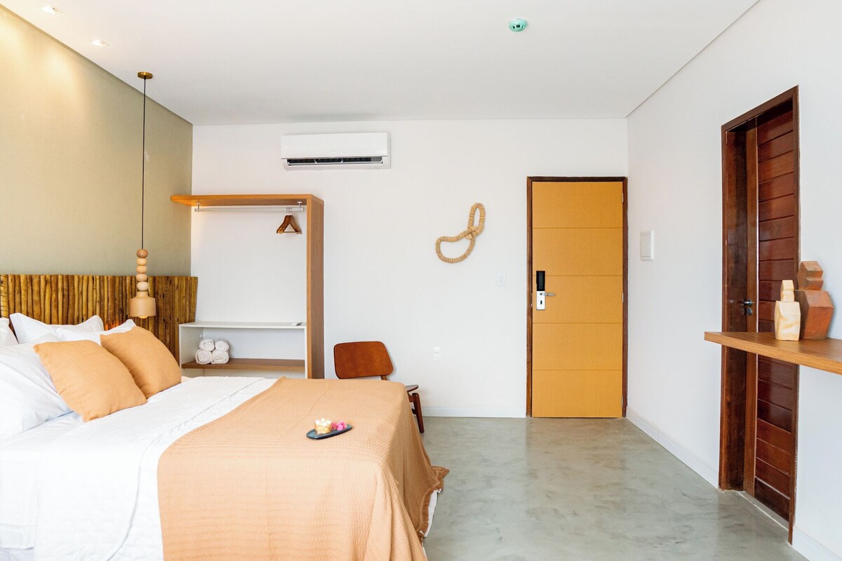 Quarto de hotel com cama, prateleira de madeira, cadeira, guarda-roupa e unidade de ar condicionado.