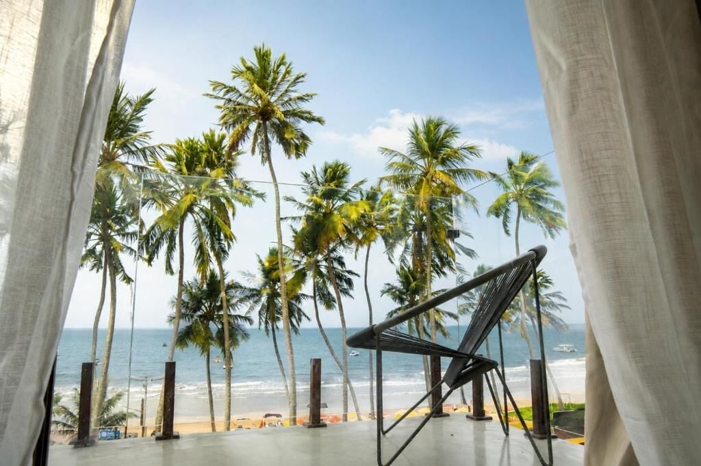 Vista da praia com palmeiras e uma cadeira.