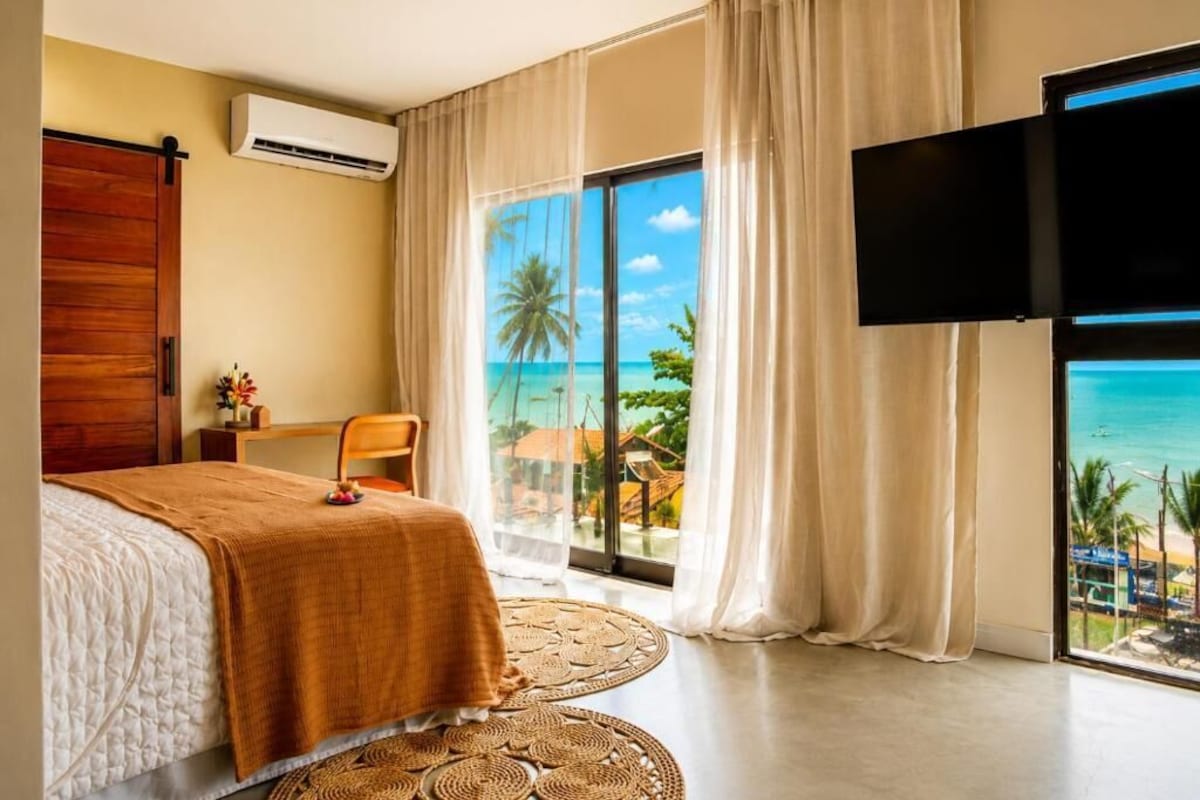 Quarto com cama, televisão, janela com vista para a praia e porta deslizante.
