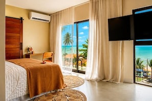 Quarto com cama, televisão, janela com vista para a praia e porta deslizante.