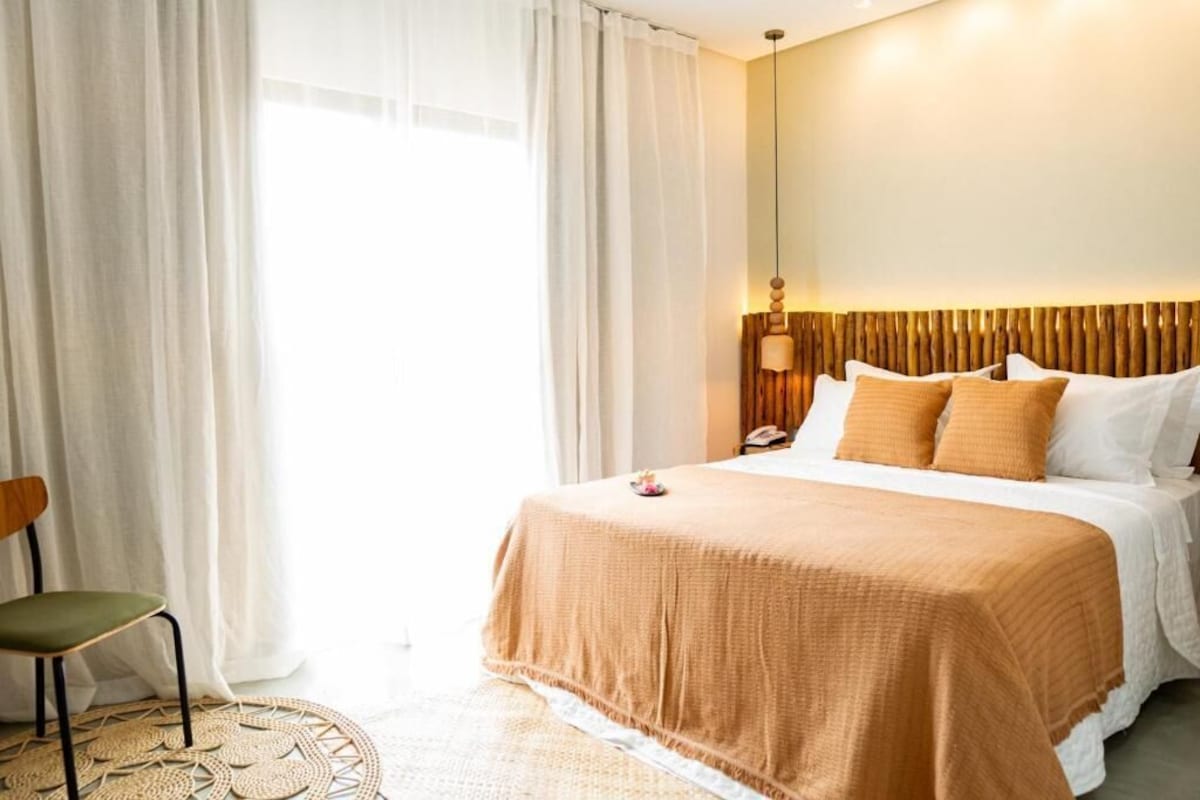 Quarto de hotel com cama, cadeira e mesa de cabeceira.
