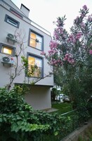Um edifício moderno com varanda, uma árvore florida com flores cor-de-rosa e um jardim bem cuidado.