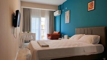 Quarto de hotel com cama, televisão na parede, janela com cortinas e vista para o exterior.