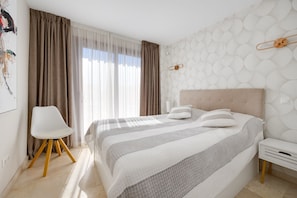 Quarto com cama, cadeira, mesa de cabeceira e parede com padrão geométrico.