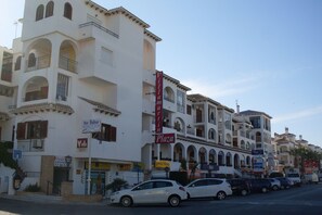 Um edifício com vários andares e varandas, um letreiro com 'Vilamar Plaza' e carros estacionados na rua.