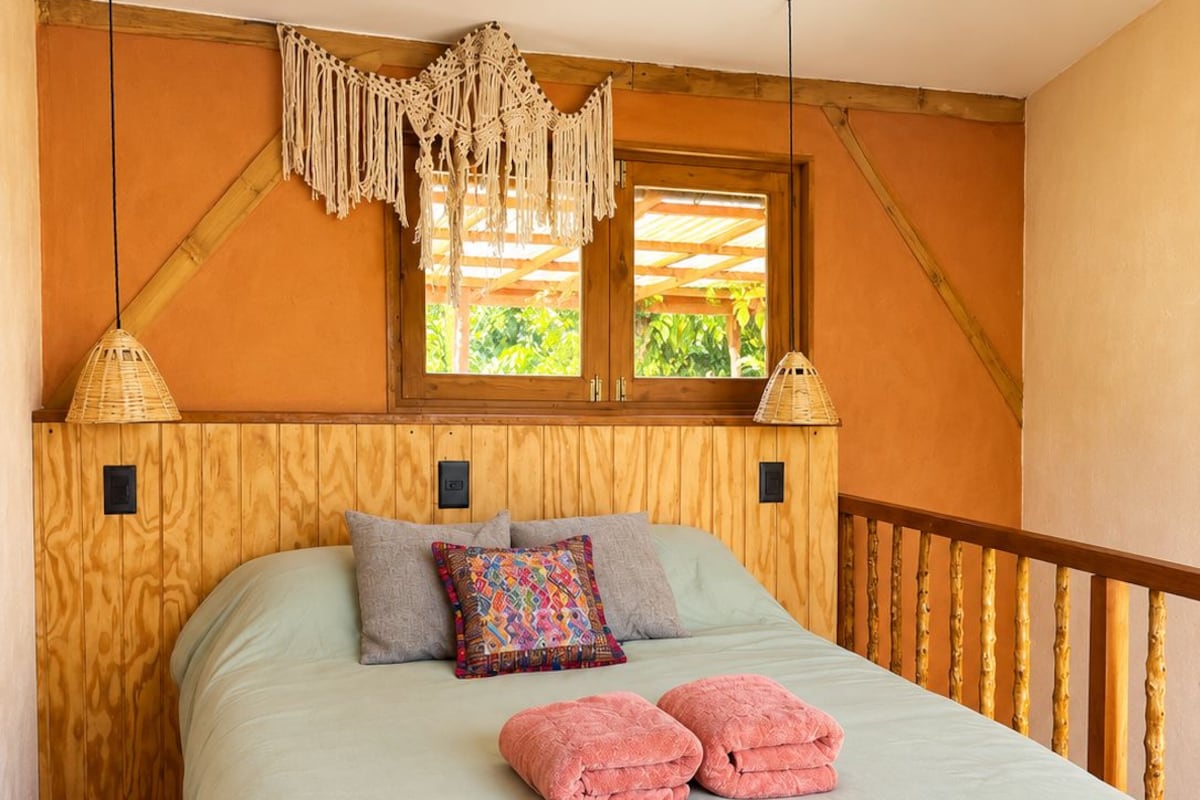 Cama com colcha verde, duas almofadas e toalhas cor-de-rosa.