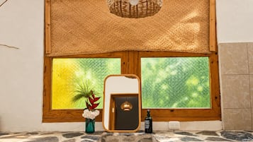 Casa de banho com lavatório de pedra, espelho, dispensador de sabonete líquido e janela com vista para vegetação.