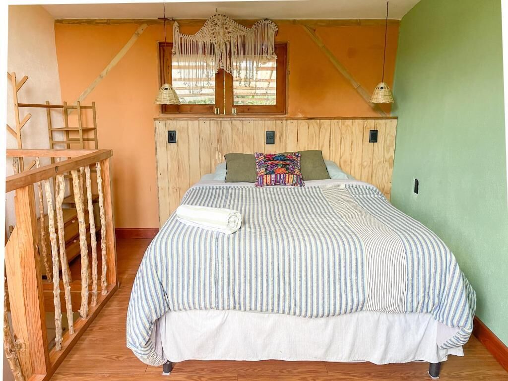 Quarto com cabeceira de madeira, cama com roupa de cama listrada, almofada colorida e corrimão de madeira.