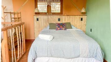 Quarto com cabeceira de madeira, cama com roupa de cama listrada, almofada colorida e corrimão de madeira.
