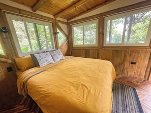 Quarto com cama, paredes de madeira e janelas amplas.