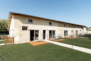 Um edifício de dois andares com telhado plano e um pátio pavimentado com móveis de exterior.