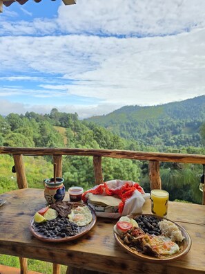 Mesa de madeira com comida de café da manhã e vista para uma paisagem montanhosa.