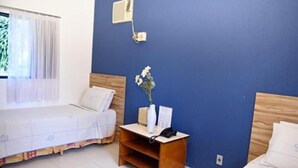 Quarto de hotel com duas camas, uma mesa de cabeceira com telefone e ar condicionado fixado na parede.