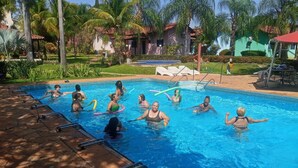 Piscina cercada por palmeiras e um edifício com telhado vermelho, com pessoas nadando.