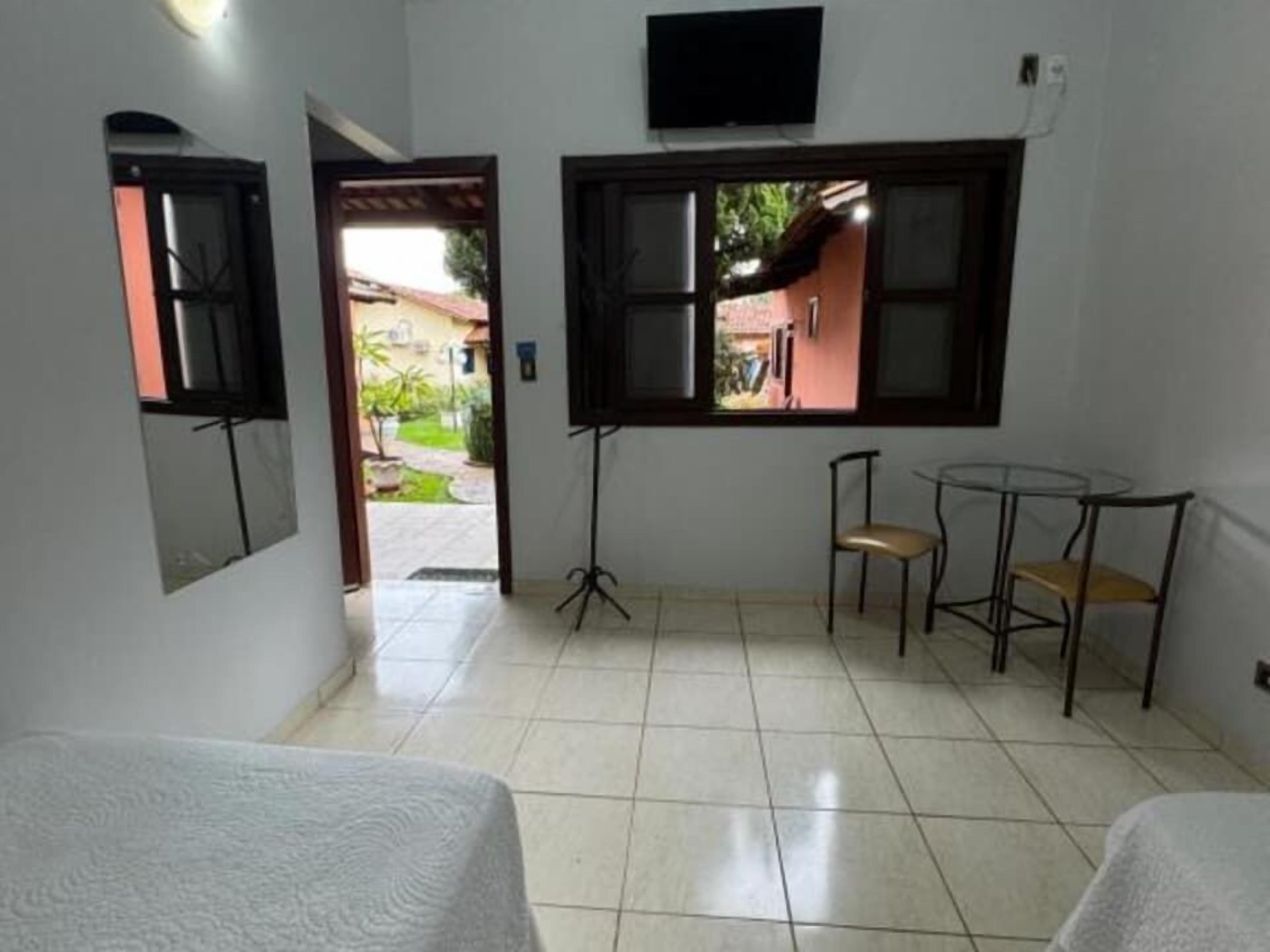 Quarto com cama, uma pequena mesa com cadeira, janela com vista para o exterior e televisão fixada na parede.