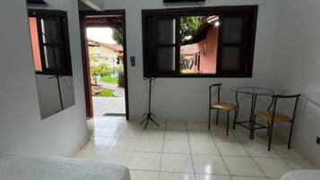 Quarto com cama, uma pequena mesa com cadeira, janela com vista para o exterior e televisão fixada na parede.