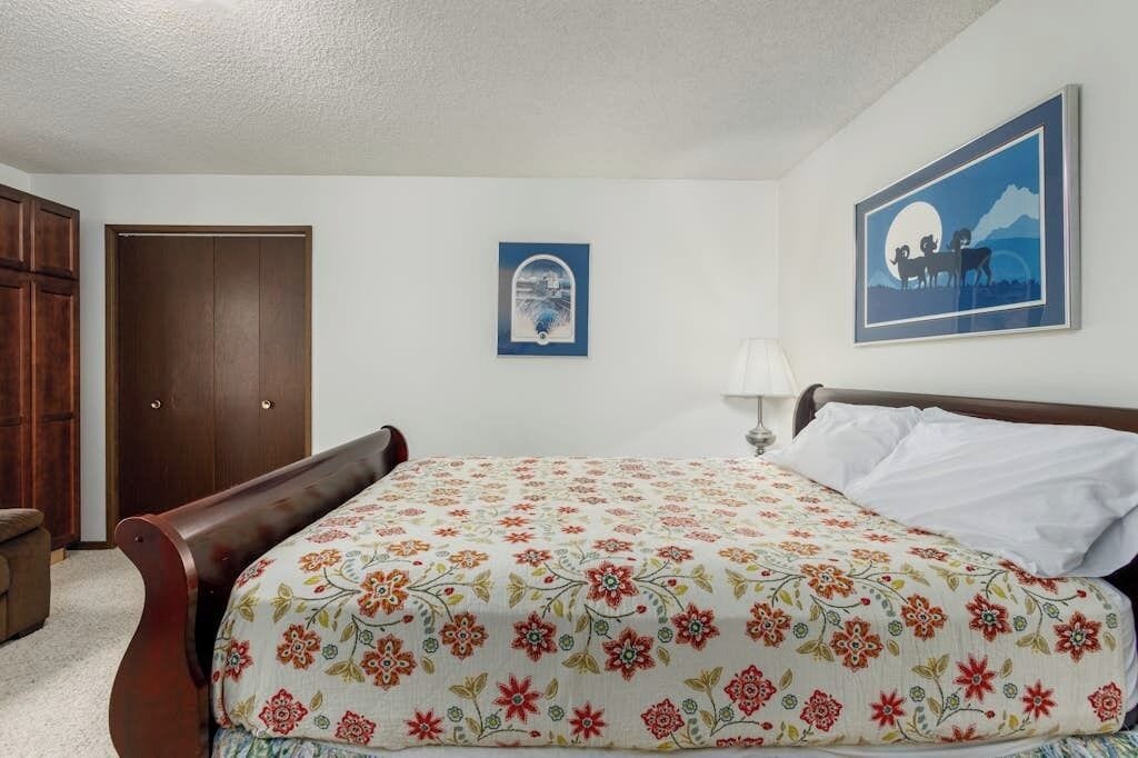 Um quarto com uma cama, uma mesinha de cabeceira, um abajur, uma porta e um quadro na parede.