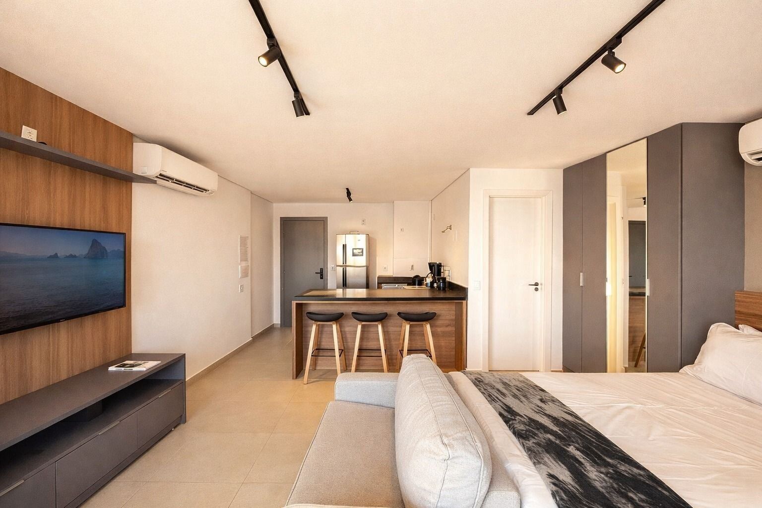 Quarto de hotel moderno com cama, televisão, cozinha e área de estar.