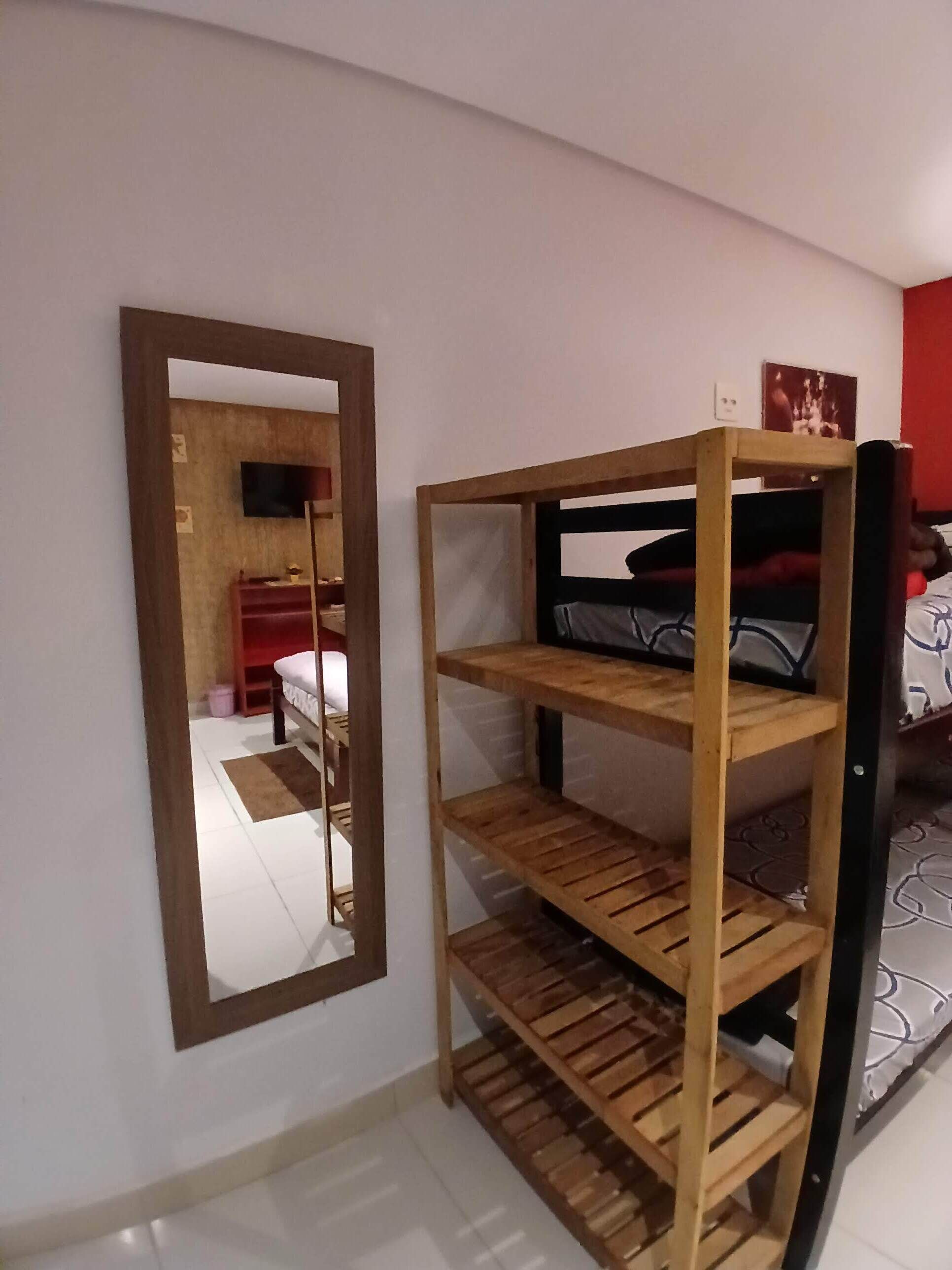 Quarto com estante de madeira encostada parede, espelho e cama com parede de destaque vermelha.