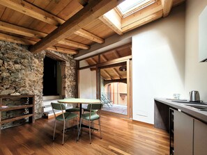 Uma sala de jantar com uma mesa e cadeiras de madeira, uma parede de pedra e vista para o exterior.